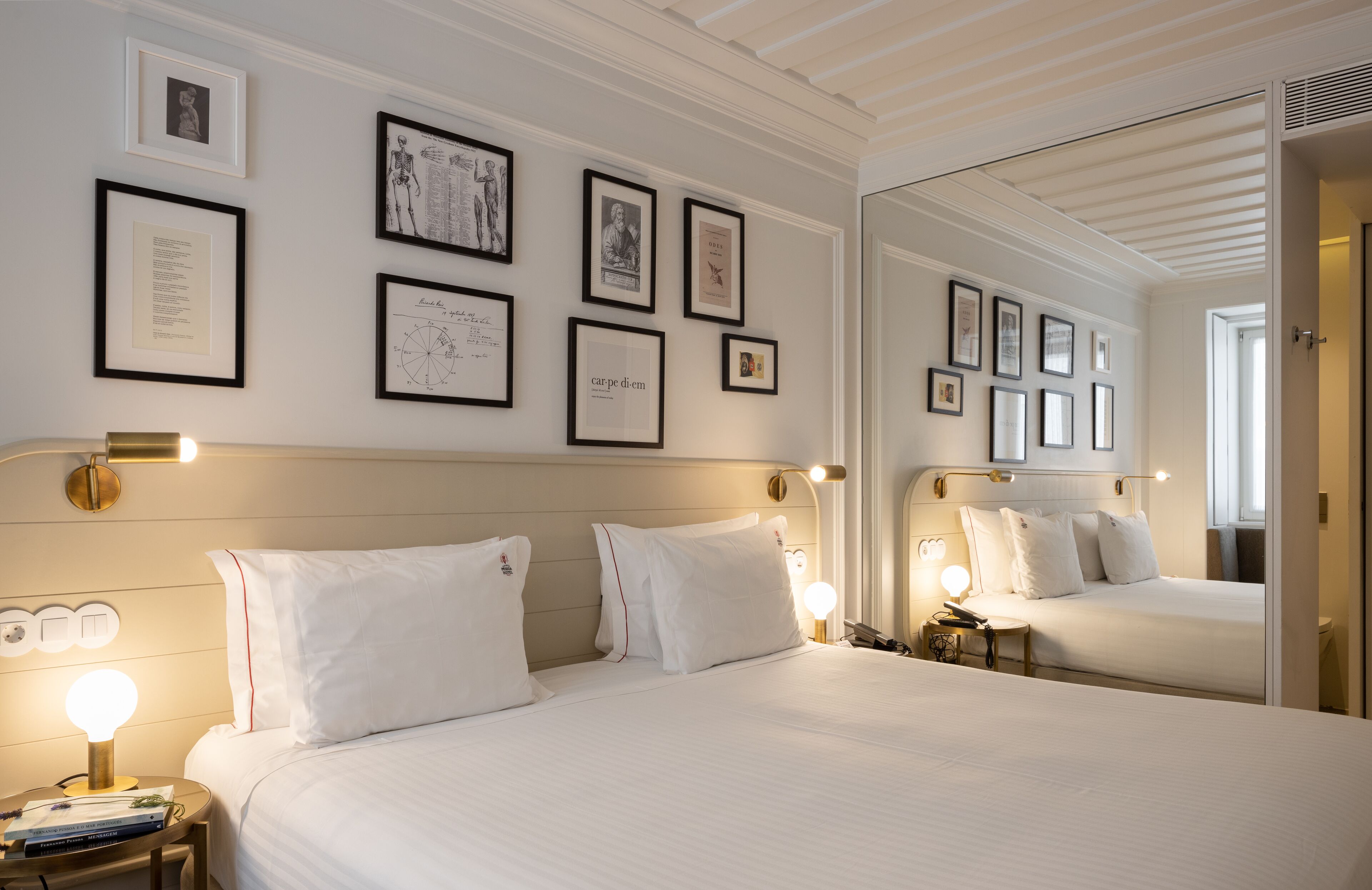 Quarto de hotel com uma cama grande, mesas de cabeceira, um espelho e quadros nas paredes.