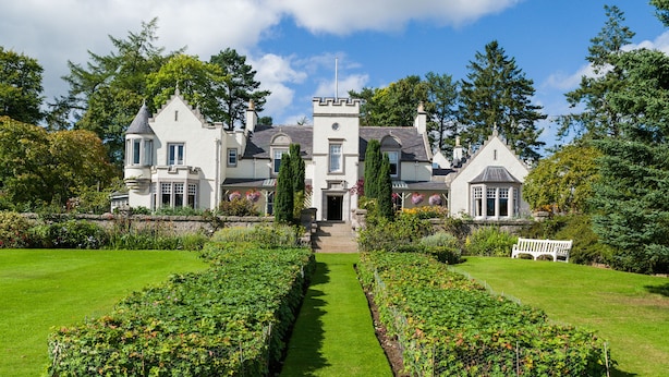 Uma casa grande e imponente com fachada simétrica, entrada central e jardim bem cuidado com sebes e gramado.