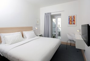 Quarto de hotel com uma cama grande, uma escrivaninha com cadeira, televisão e janela com cortinas.