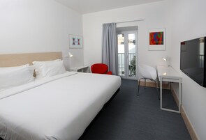 Quarto de hotel com cama, escrivaninha, televisão, poltrona e varanda com vista.