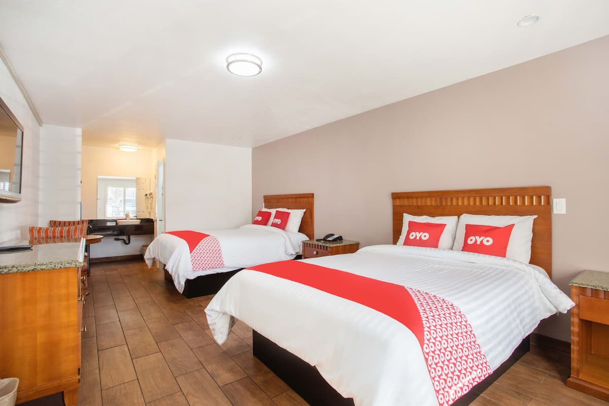 Quarto de hotel com duas camas, uma cabeceira de madeira, uma escrivaninha e um espelho.