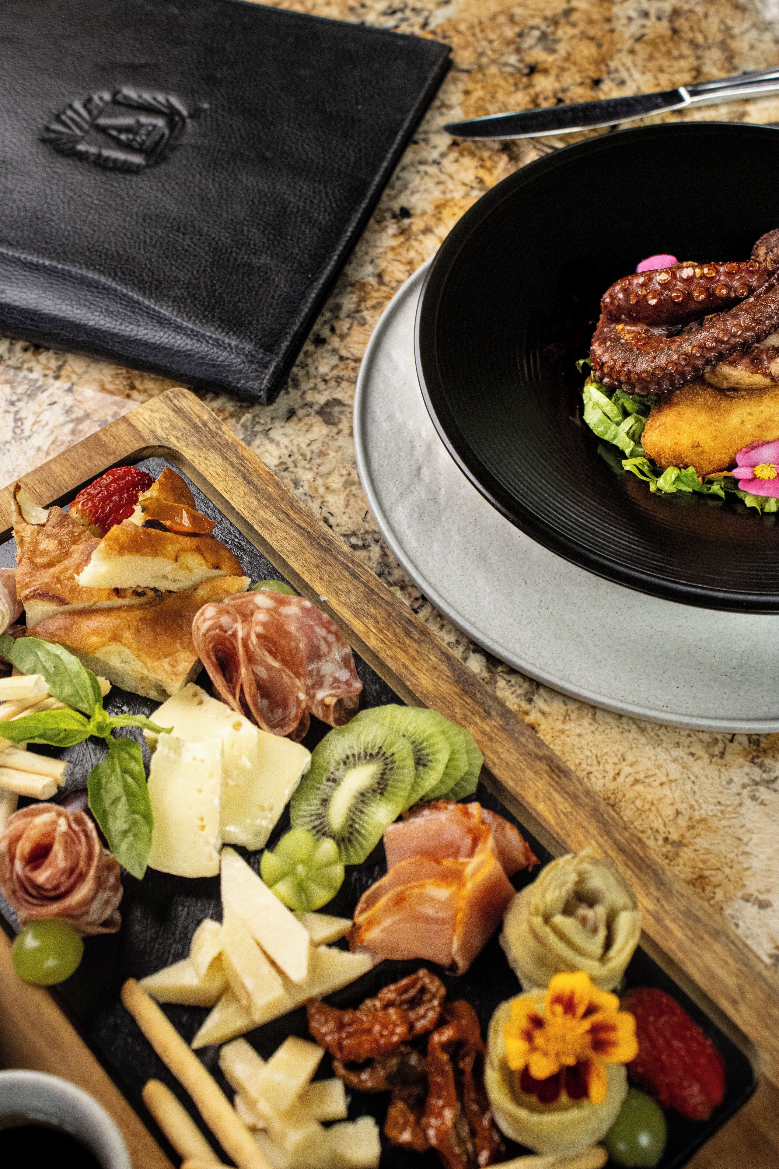 Tábua de frios com diversos queijos, carnes e frutas sobre uma tábua de madeira.