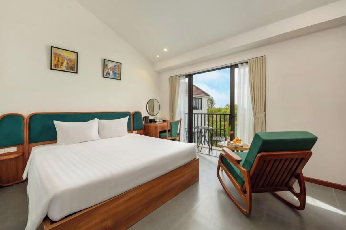 Quarto de hotel com uma cama grande, uma escrivaninha com cadeira e uma varanda com vista.