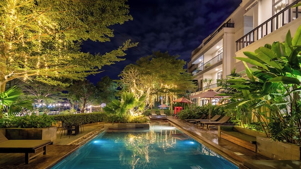 Uma área de piscina à noite, com espreguiçadeiras e um caminho bem iluminado.