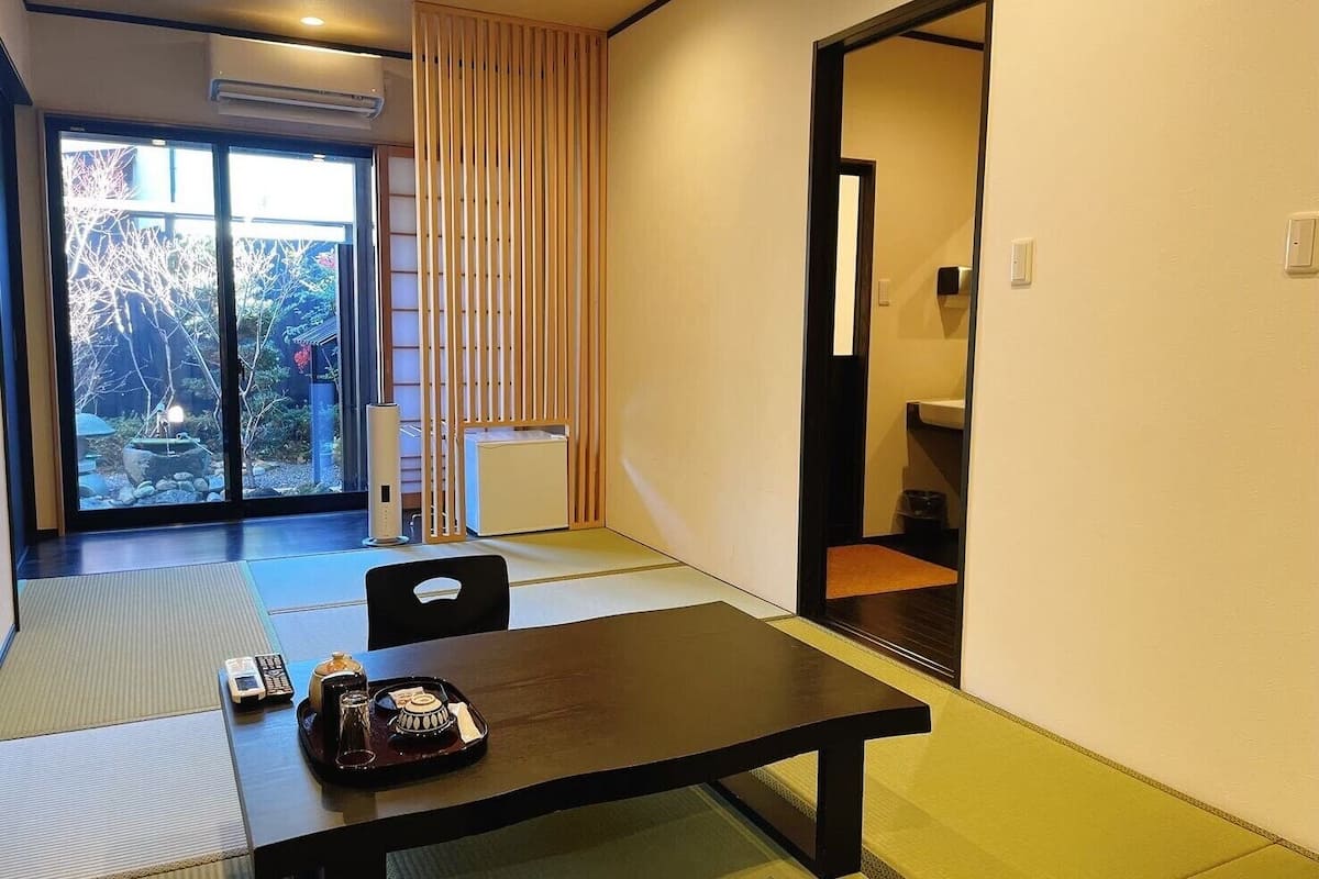 Quarto com esteiras de tatame, uma mesa baixa, uma porta de correr e vista para um jardim.