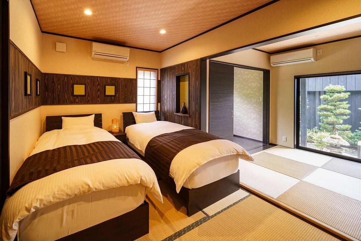 Quarto de hotel com duas camas, porta deslizante para uma varanda e estética japonesa tradicional.