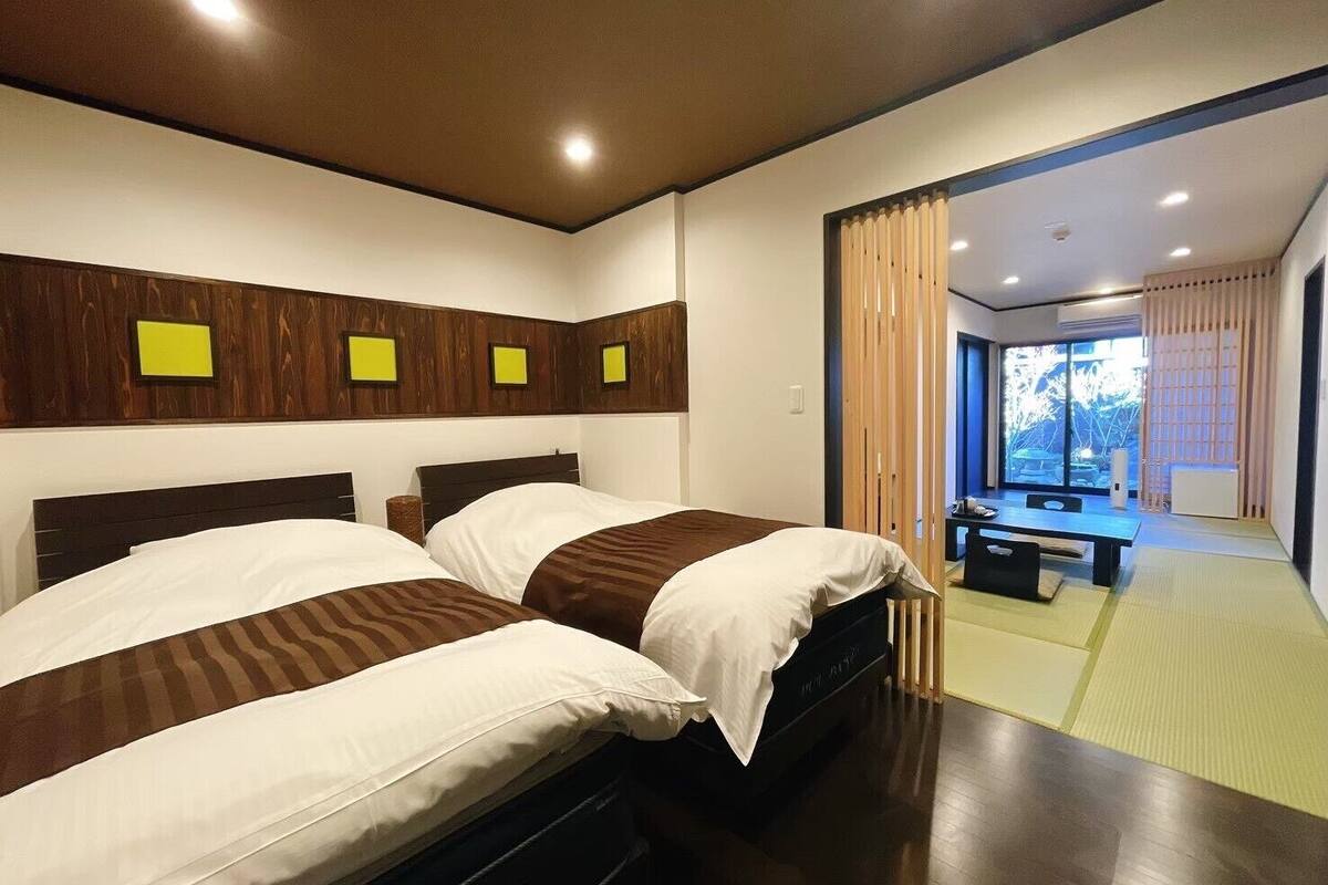 Quarto de hotel moderno com duas camas, cabeceira de madeira e vista exterior através de amplas janelas.
