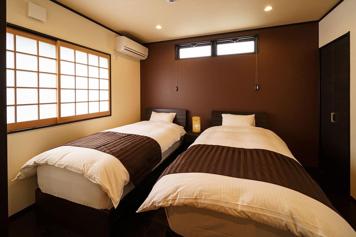 Quarto de hotel com duas camas, uma janela, ar condicionado e uma porta.