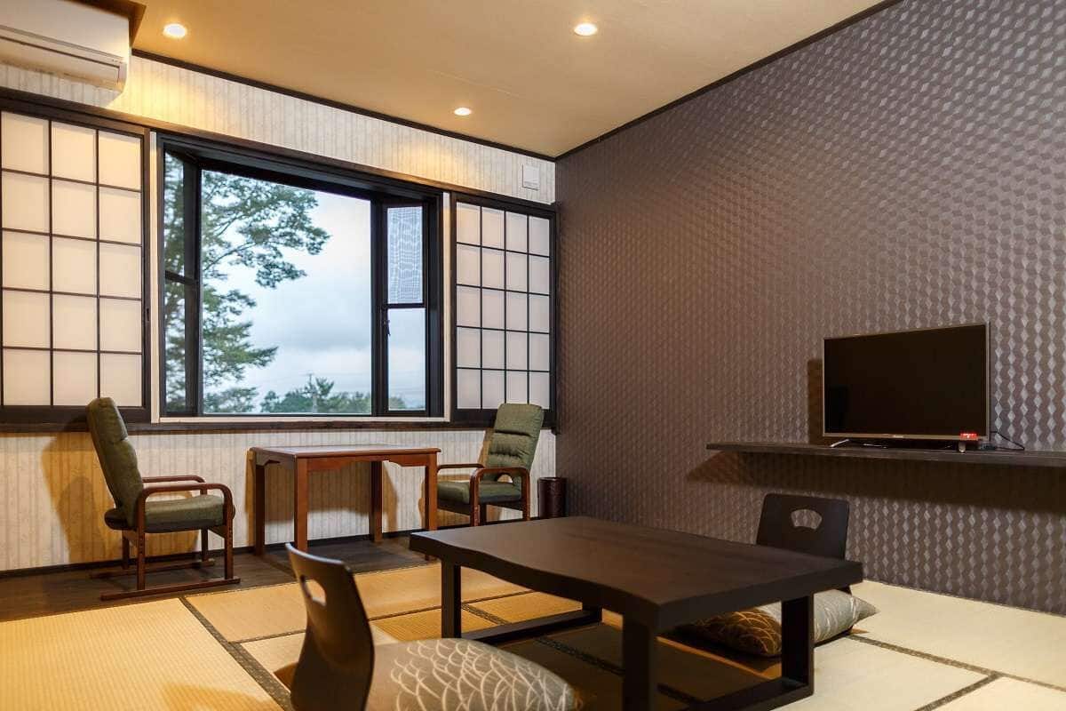 Quarto em estilo japonês tradicional, com tatames, uma mesa baixa e cadeiras.