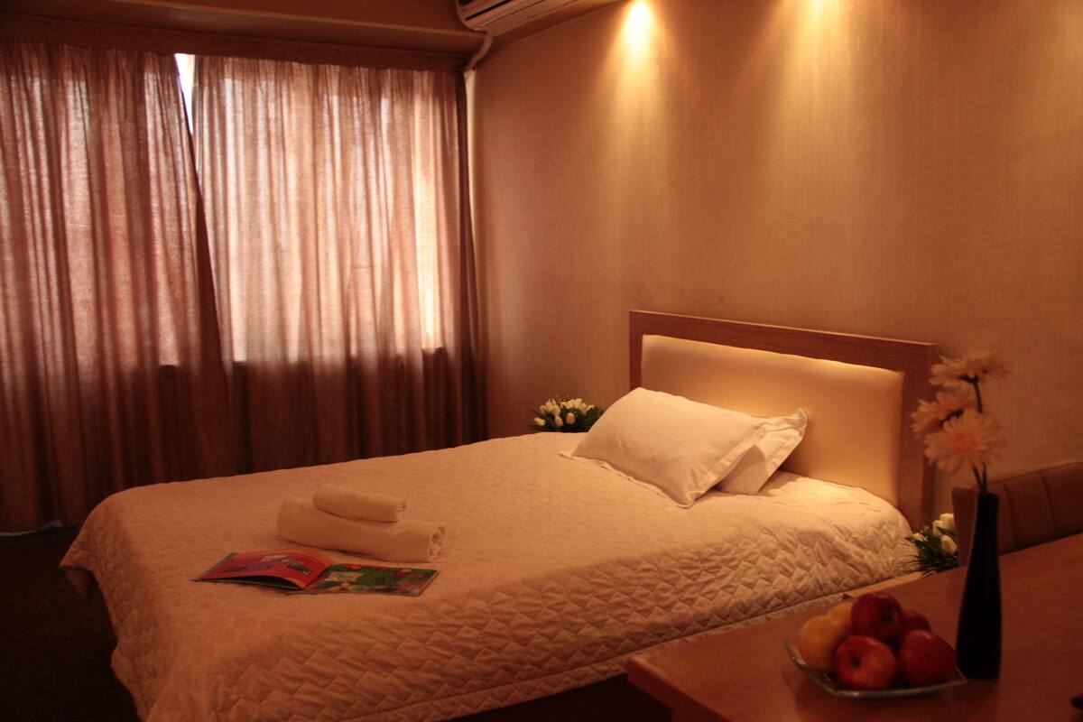 Quarto de hotel com uma cama, uma mesa de cabeceira com um vaso de flores e uma cesta de frutas.