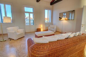 Quarto com sofá branco, sofá de vime, luminária de chão e espelho na parede.