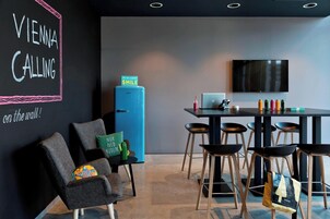 Um interior moderno com uma parede de lousa exibindo a frase 'VIENNA CALLING', uma geladeira azul, um espaço de bar com banquetas e uma TV de tela plana.