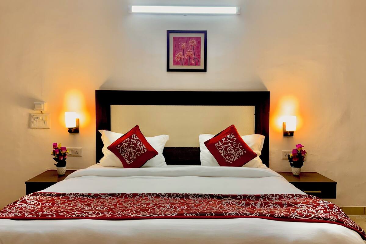Quarto de hotel com uma cama grande, duas mesas de cabeceira, uma obra de arte emoldurada acima da cama e luminárias fixadas na parede.