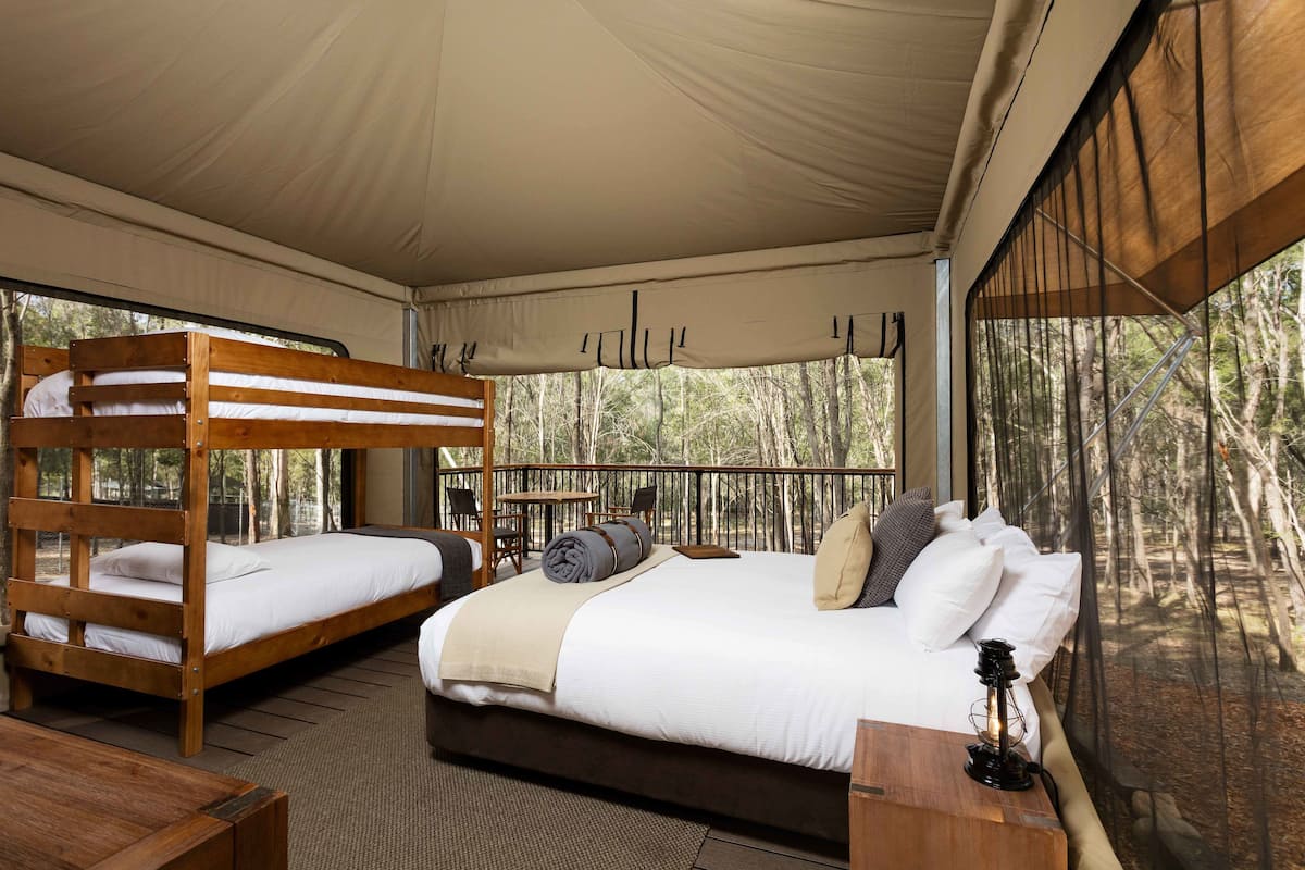 Alojamento tipo tenda com uma cama de beliche, uma cama individual e uma mesa.