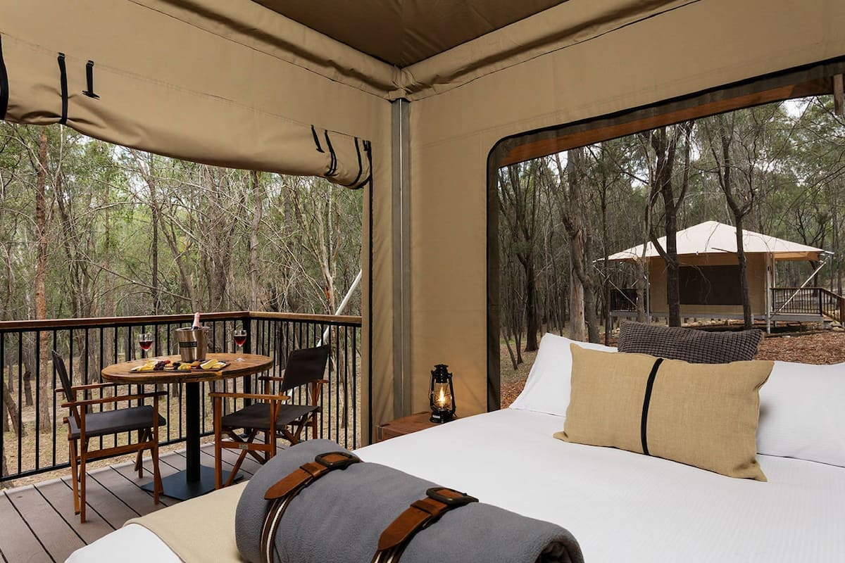 Quarto com cama grande, mesa e cadeiras, e vista para a floresta.