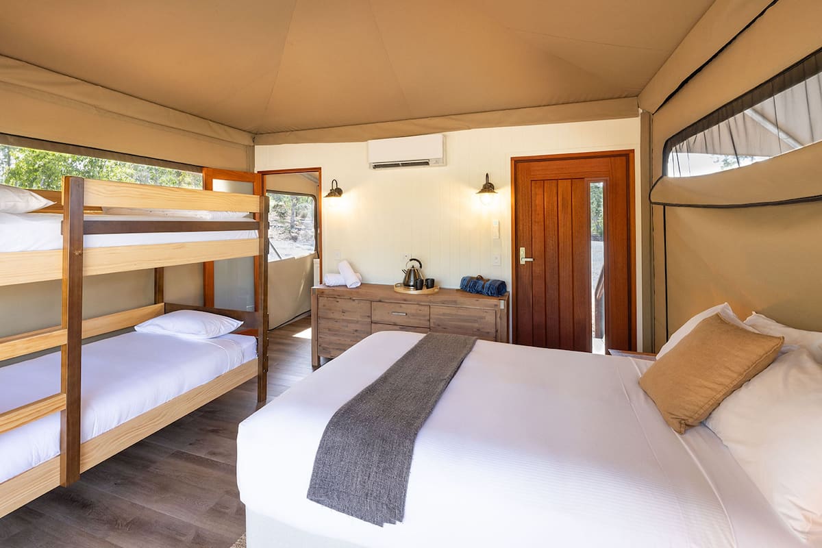 Quarto com beliches, cômoda de madeira, mesa de cabeceira e porta que dá para o exterior.