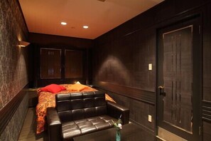 Um quarto com uma cama, um sofá de couro preto, uma porta de madeira e um aplique na parede.