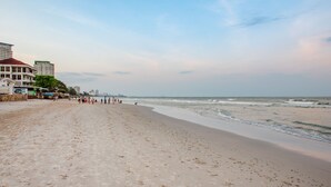 Uma praia com areal, algumas pessoas e edifícios ao fundo.