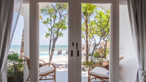 Vista de um quarto com porta de vidro para uma área de praia, incluindo cadeiras de vime e uma pequena piscina.