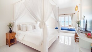 Quarto com cama de dossel, mesa de cabeceira com um vaso e vista para o mar através de grandes janelas.