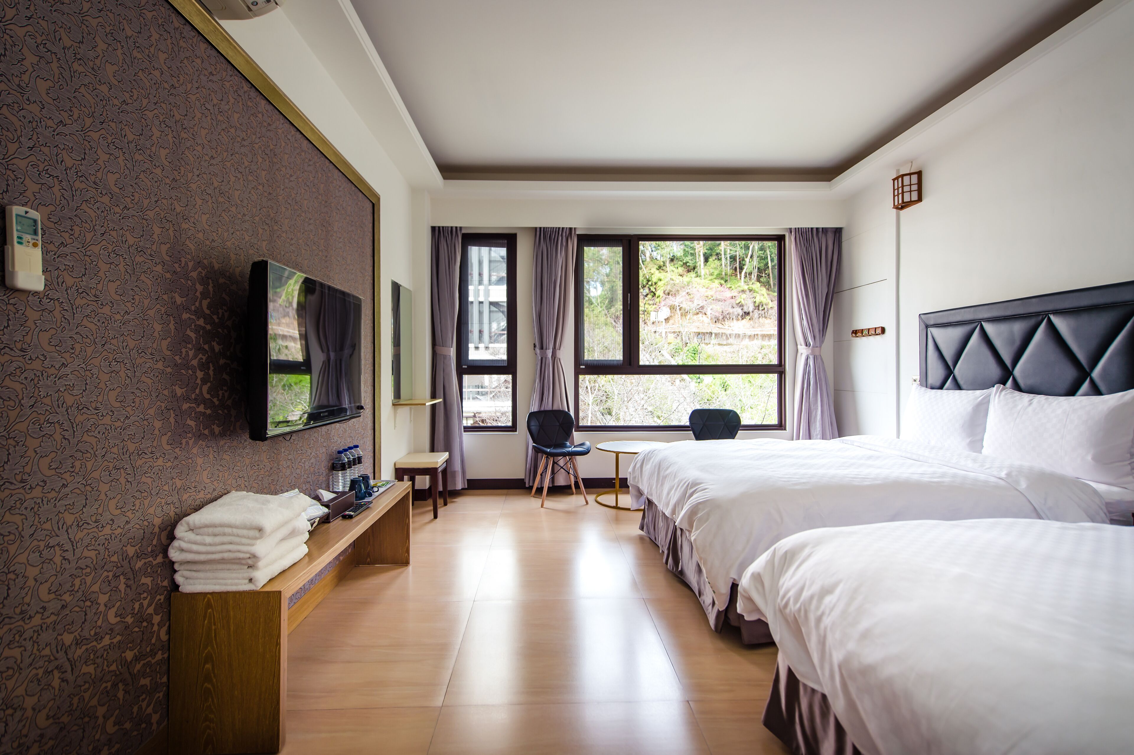 Quarto de hotel com duas camas, televisão, escrivaninha com cadeira e janela com cortinas.