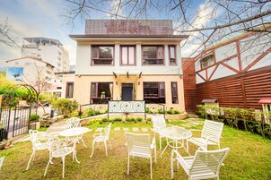 Uma casa de dois andares com jardim frontal e área de estar ao ar livre.