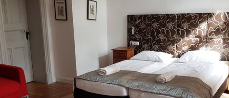 Quarto com cama, mesa de cabeceira, cadeira vermelha e uma porta.