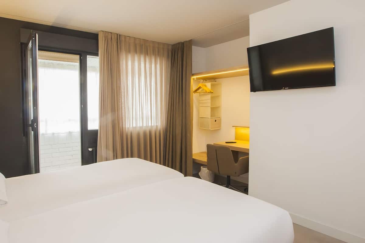 Quarto de hotel com cama, secretária, cadeira, televisão e guarda-roupa.