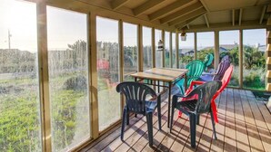 Varanda coberta com mesa e cadeiras, janelas amplas e vista para vegetação e colinas.