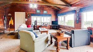 Interior acolhedor de cabana com teto de madeira, sofá, mesa de centro, televisão e lareira.