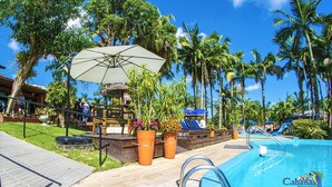 Uma área de piscina com espreguiçadeira, um grande guarda-sol e um bar à beira da piscina.