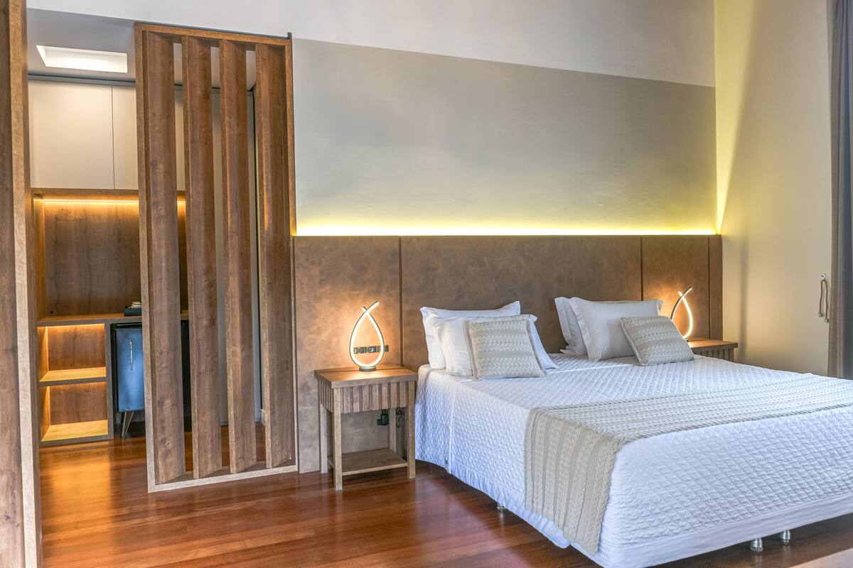 Quarto moderno com uma cama grande, mesas de cabeceira de madeira e uma escrivaninha embutida com abajur.