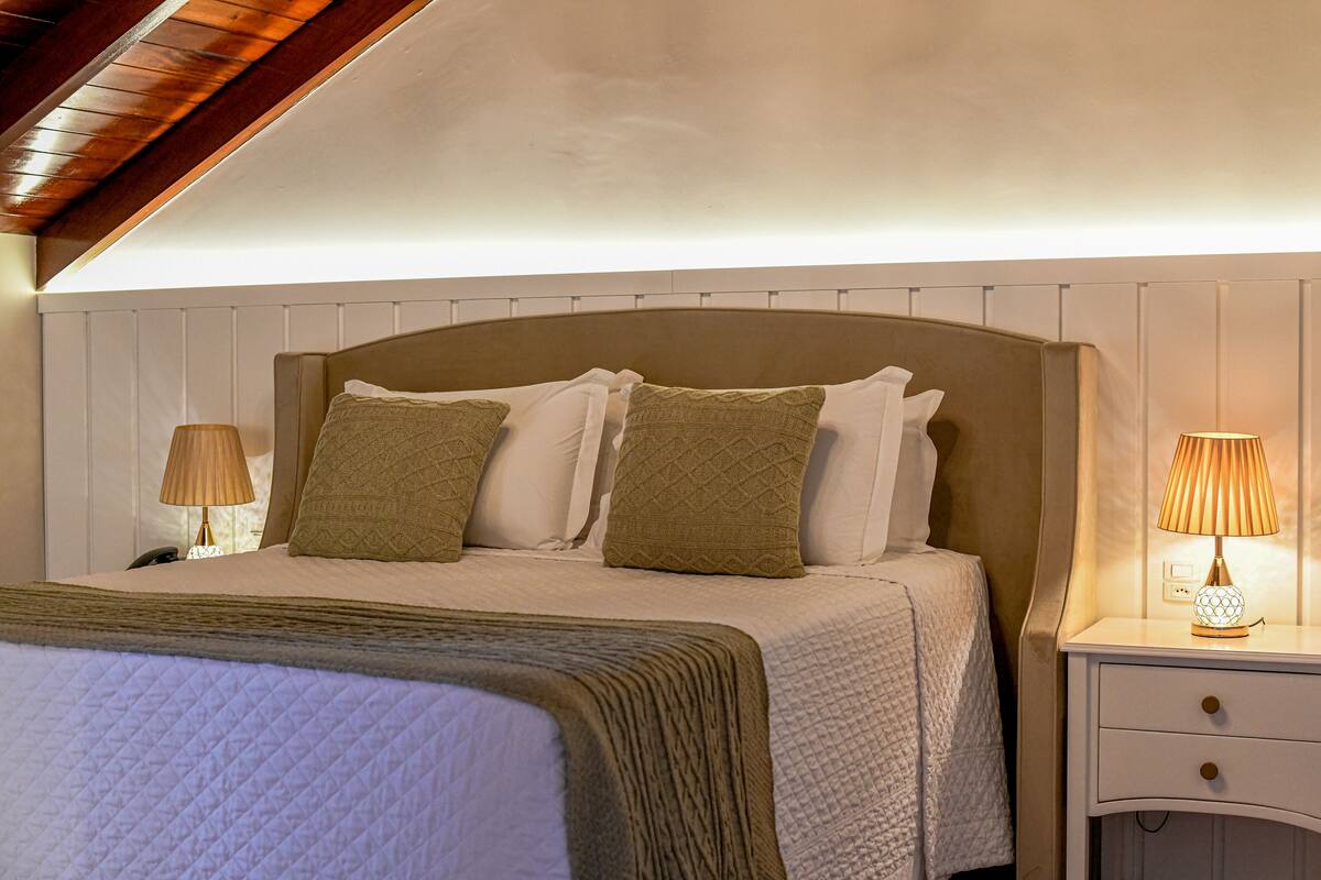 Cama bem arrumada com cabeceira, duas luminárias de cabeceira e mesa de cabeceira com abajur.