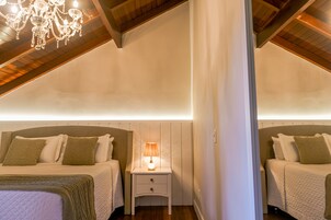 Quarto com duas camas, mesa de cabeceira com abajur e lustre.