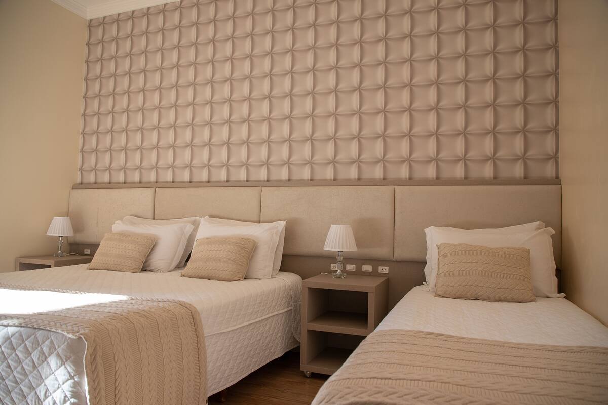 Quarto de hotel com duas camas, cada uma com cabeceira, mesas de cabeceira, abajures e colcha acolchoada.