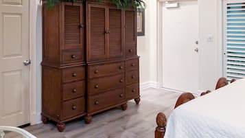 Quarto com cômoda de madeira, cama com colcha branca e porta com janela.