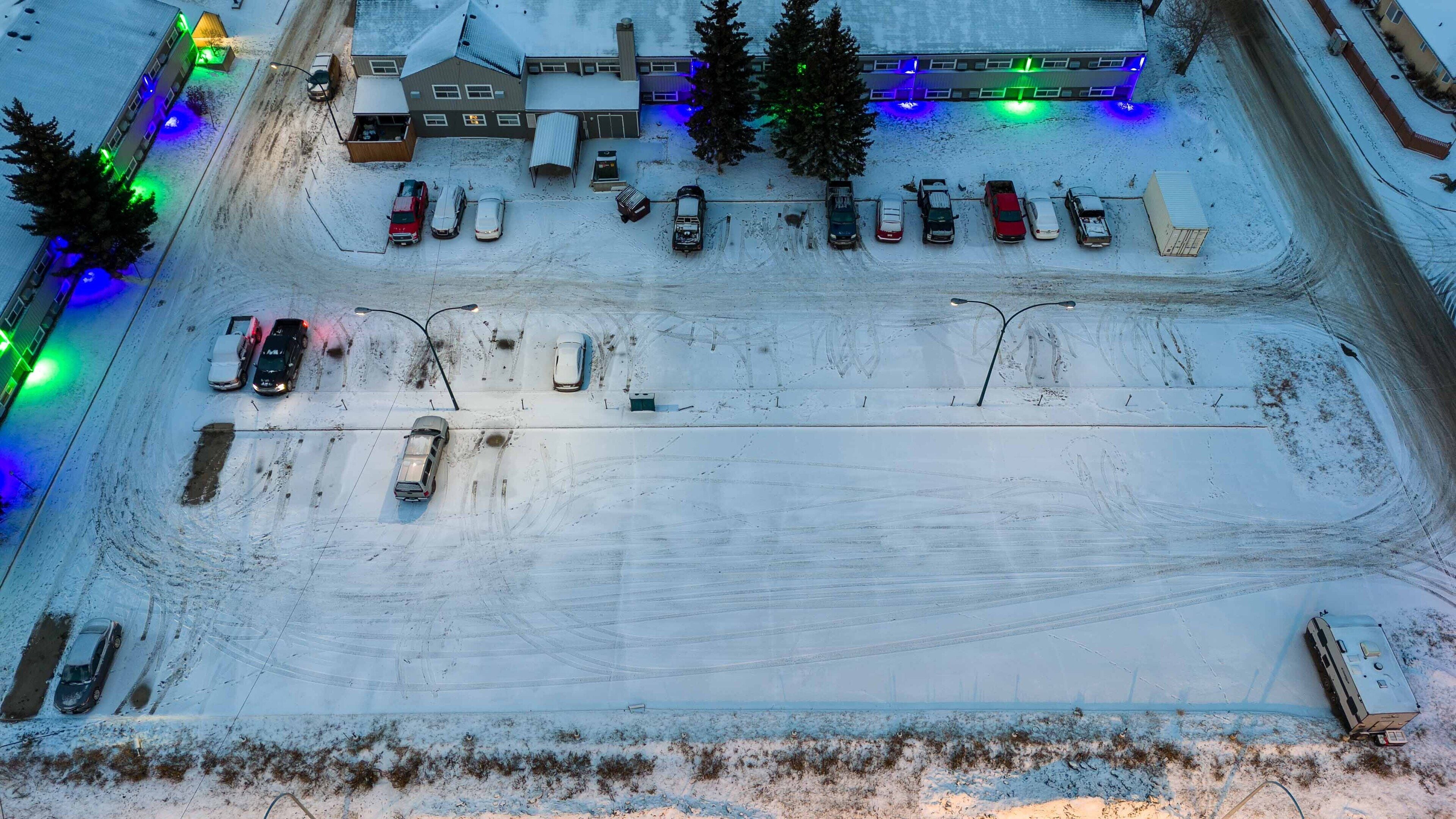 Vista aérea de um estacionamento com vários carros, um edifício com telhado inclinado e uma grande árvore.