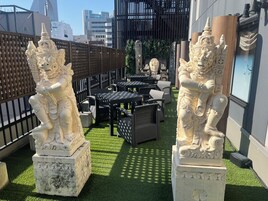 Um terraço no telhado com duas estátuas de pedra, mobiliário de exterior e vista para a paisagem urbana.