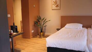 Quarto de hotel com cama, escrivaninha, planta em vaso e quadro pendurado na parede.