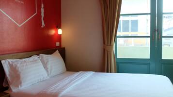 Quarto de hotel com cama, uma parede com pôster, janela com cortinas e mesa de cabeceira.