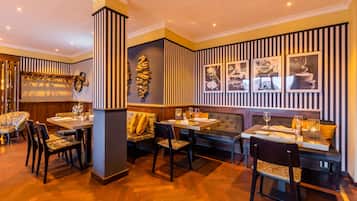 Restaurante com piso de madeira, paredes listradas e diversos assentos, incluindo mesas e bancos.