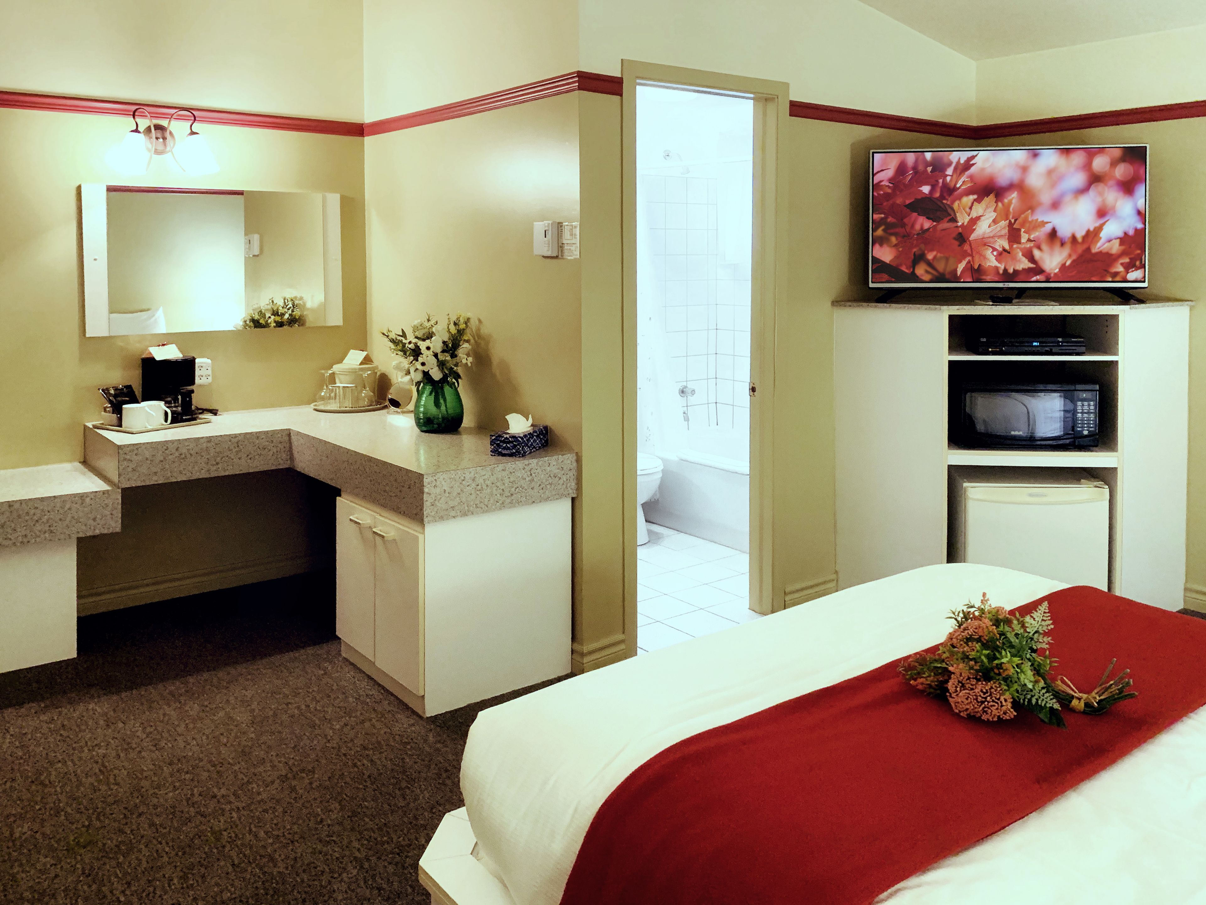 Quarto de hotel com uma cama, televisão, micro-ondas, máquina de café e casa de banho visível através de uma porta aberta.