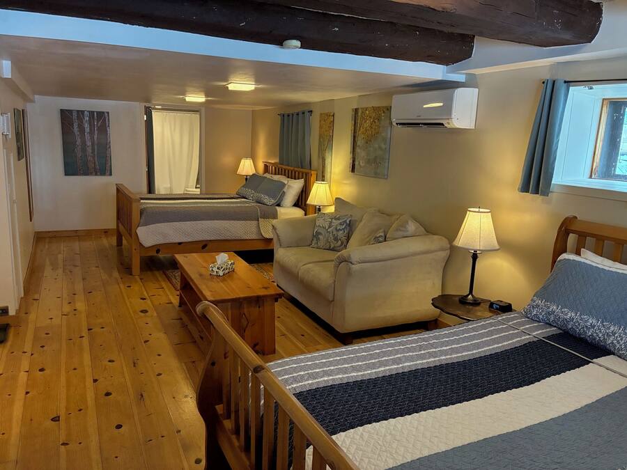 Um quarto aconchegante com duas camas, um sofá, uma mesa de madeira e uma luminária.