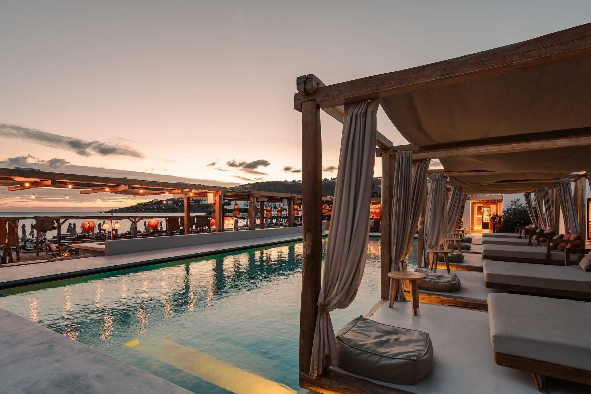 Área de piscina no terraço, com assentos e vista da cidade ao pôr do sol.