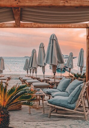 Um espaço de descanso à beira-mar, com cadeiras e guarda-sóis de madeira, com vista para o mar.