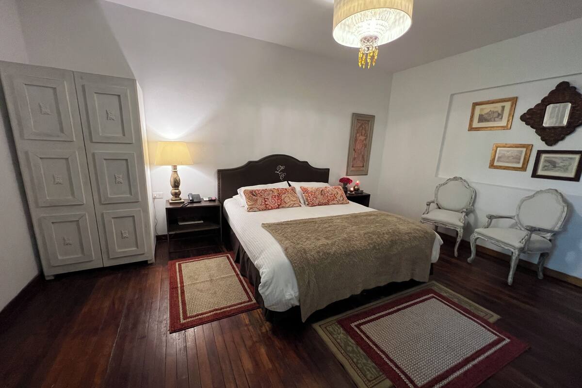 Quarto com cama, mesas de cabeceira, abajur, candelabro e uma cadeira.