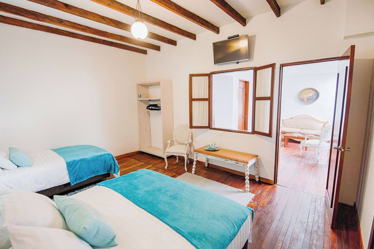 Quarto com duas camas, teto de madeira, televisão, espelho e porta que dá para uma varanda.