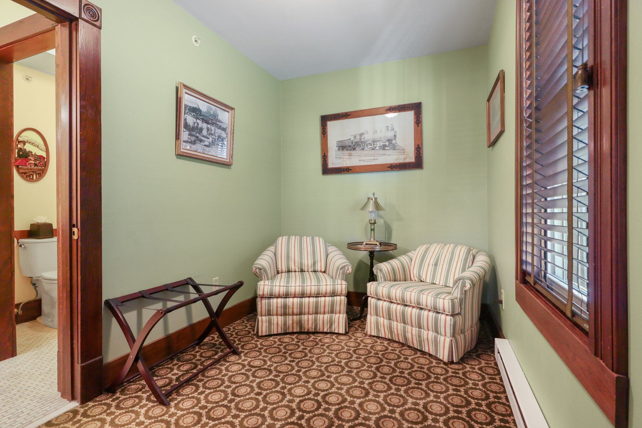 Um quarto com duas poltronas listradas, uma mesa pequena e duas imagens emolduradas na parede.