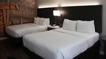 Quarto de hotel com duas camas de solteiro, uma escrivaninha com luminária e uma cadeira.