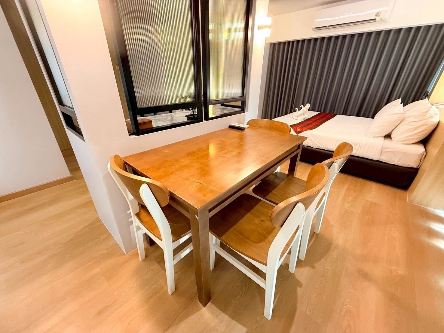Quarto moderno com mesa de jantar de madeira e quatro cadeiras, um sofá e uma janela grande com persianas.